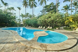 Uma piscina com design curvo singular, cercada por palmeiras e espreguiçadeiras.