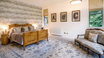 Quarto com cama de madeira, um sofá, tapete estampado e gravuras botânicas emolduradas na parede.