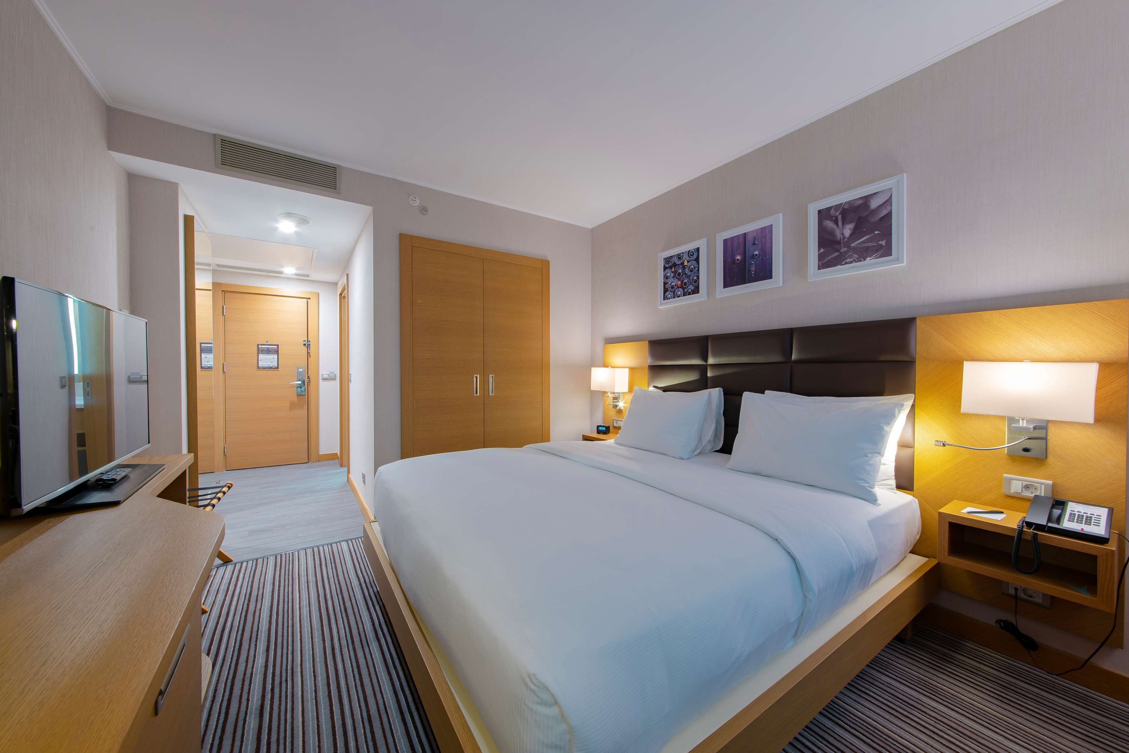 Quarto de hotel com uma cama grande, mesas de cabeceira com abajures, uma televisão e um guarda-roupa de madeira.