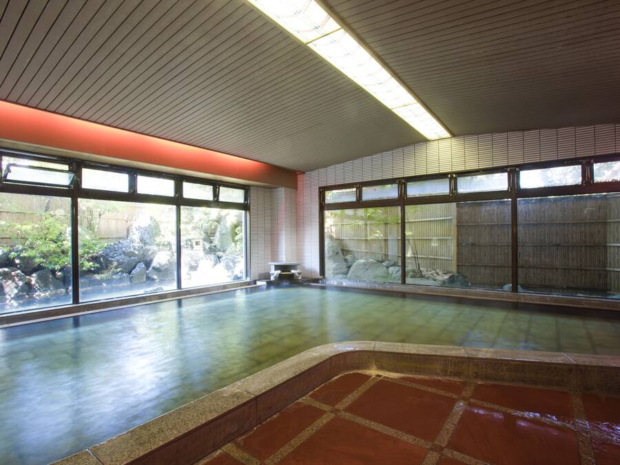 Uma grande piscina interior com janelas amplas, piso em azulejo e borda de pedra.