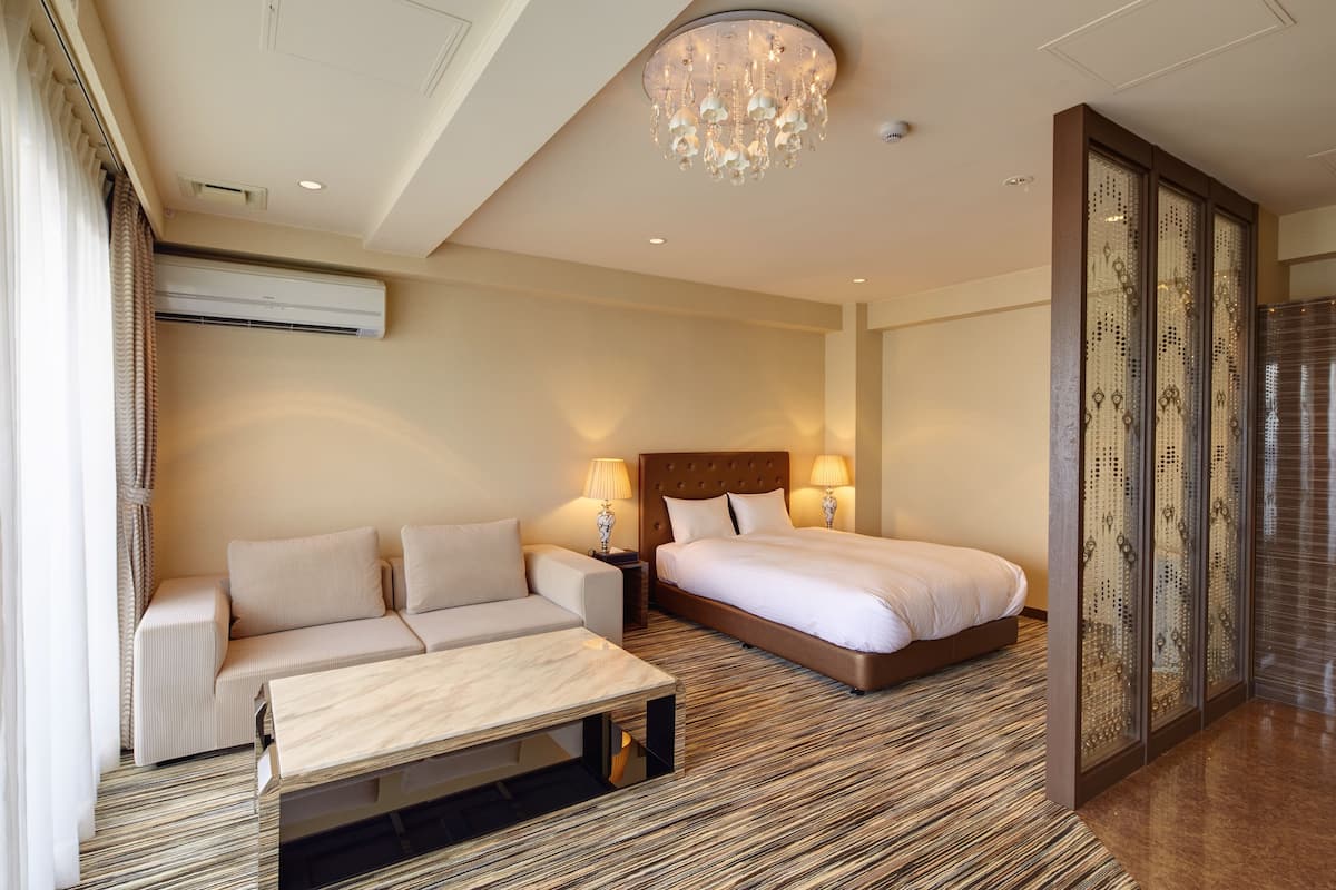 Quarto de hotel com cama, sofá, mesa de centro, candelabro e um ecrã decorativo.
