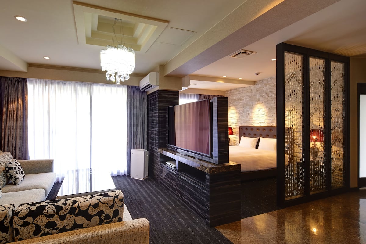 Quarto de hotel com sofá, televisão, cama e divisória decorativa.