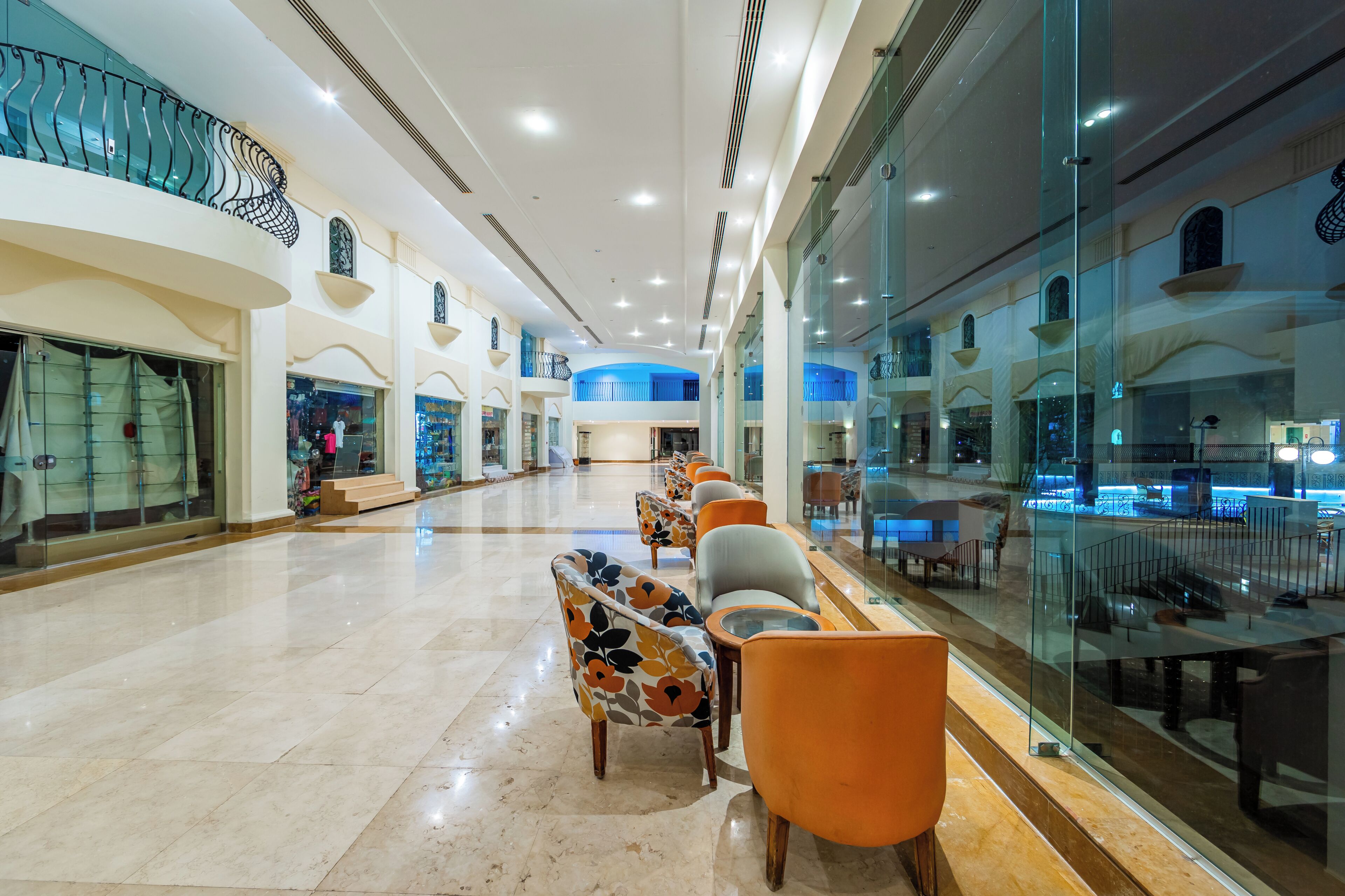 Um hall amplo com teto alto, guarda-corpo de vidro e uma fileira de cadeiras.