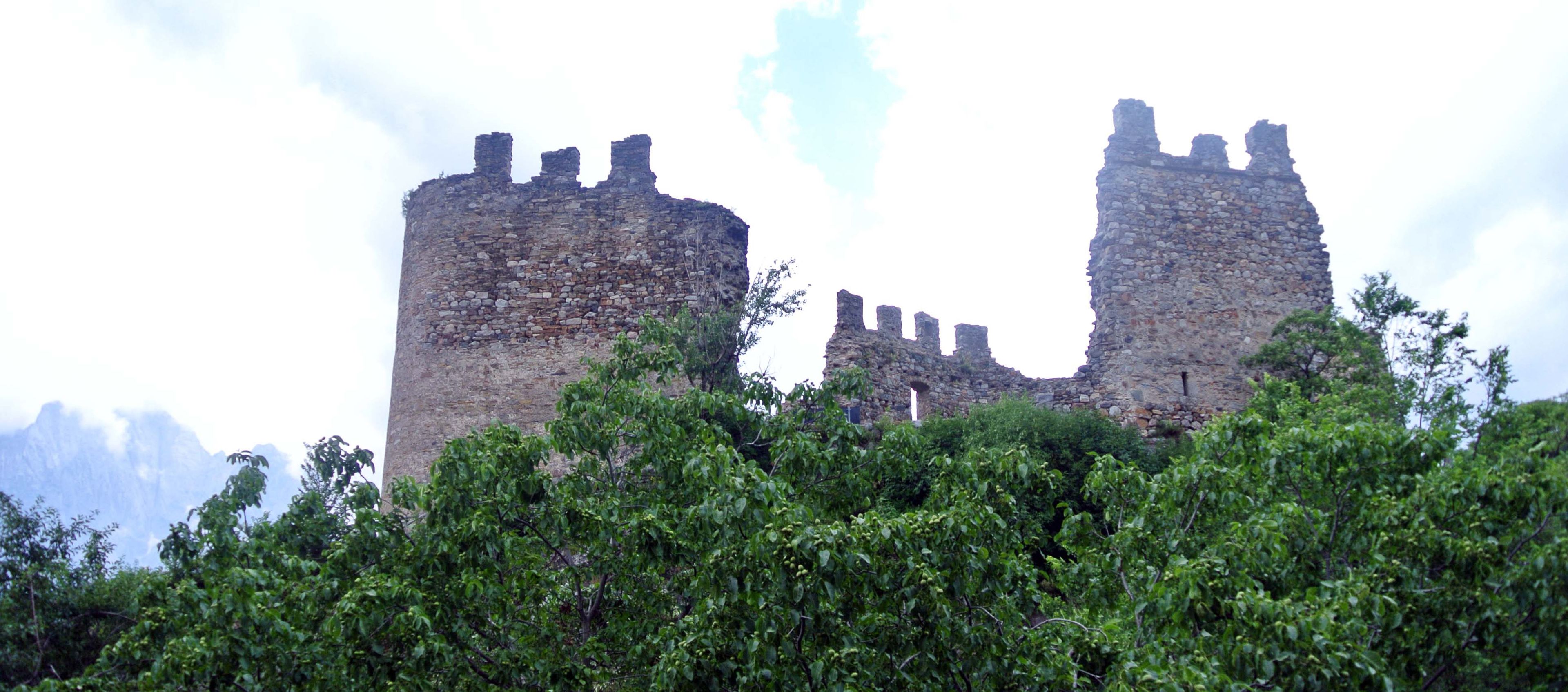 Uma torre de pedra histórica com ameias, rodeada por vegetação verde densa.