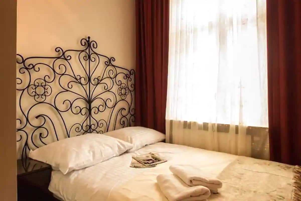 Cama bem arrumada com cabeceira metálica decorativa, lençóis brancos e uma revista sobre a cama.