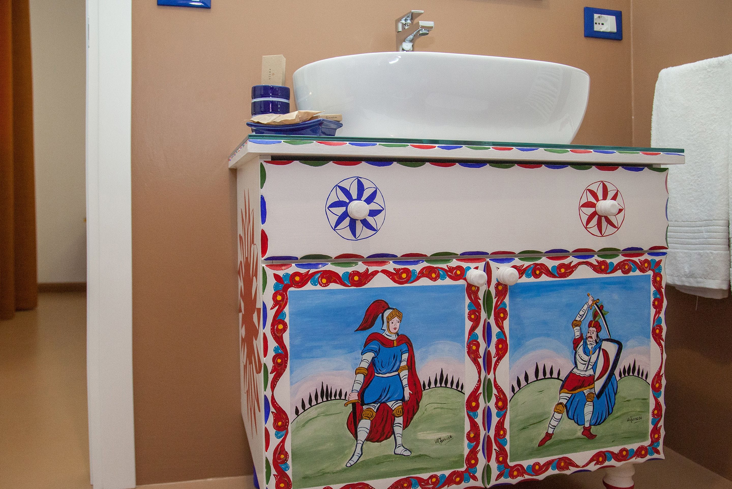 Casa de banho com lavatório branco e armário decorativo com duas pinturas de cavaleiros.