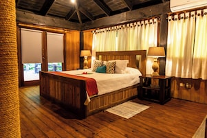 Quarto com piso de madeira, uma cama grande, duas luminárias de cabeceira e vista para o exterior por uma porta deslizante.