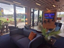 Uma área de estar moderna com sofá, poltronas, televisão e grandes janelas com vista para a paisagem urbana.