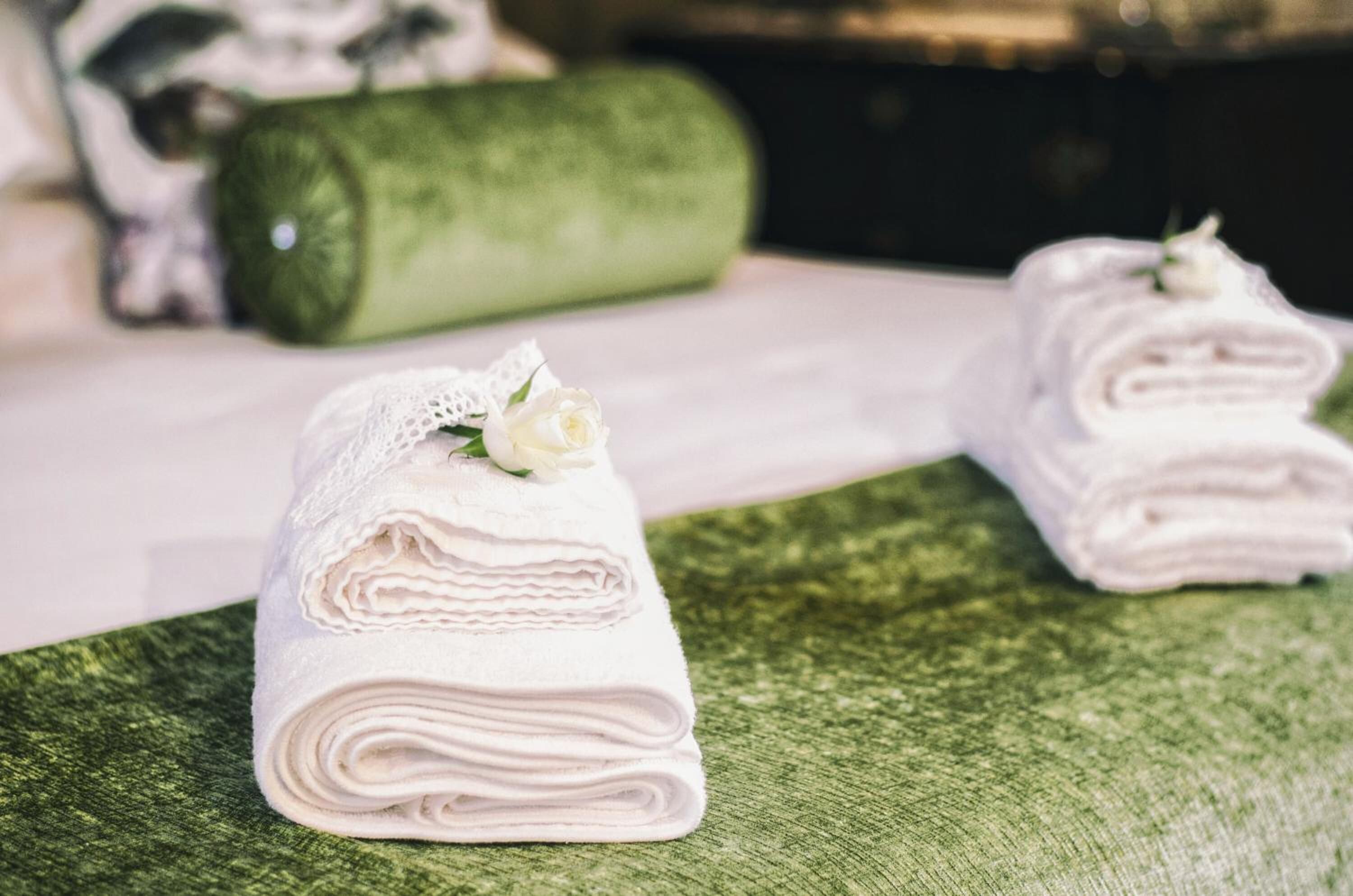Toalhas brancas dobradas com renda e uma flor branca sobre uma superfície verde texturizada.