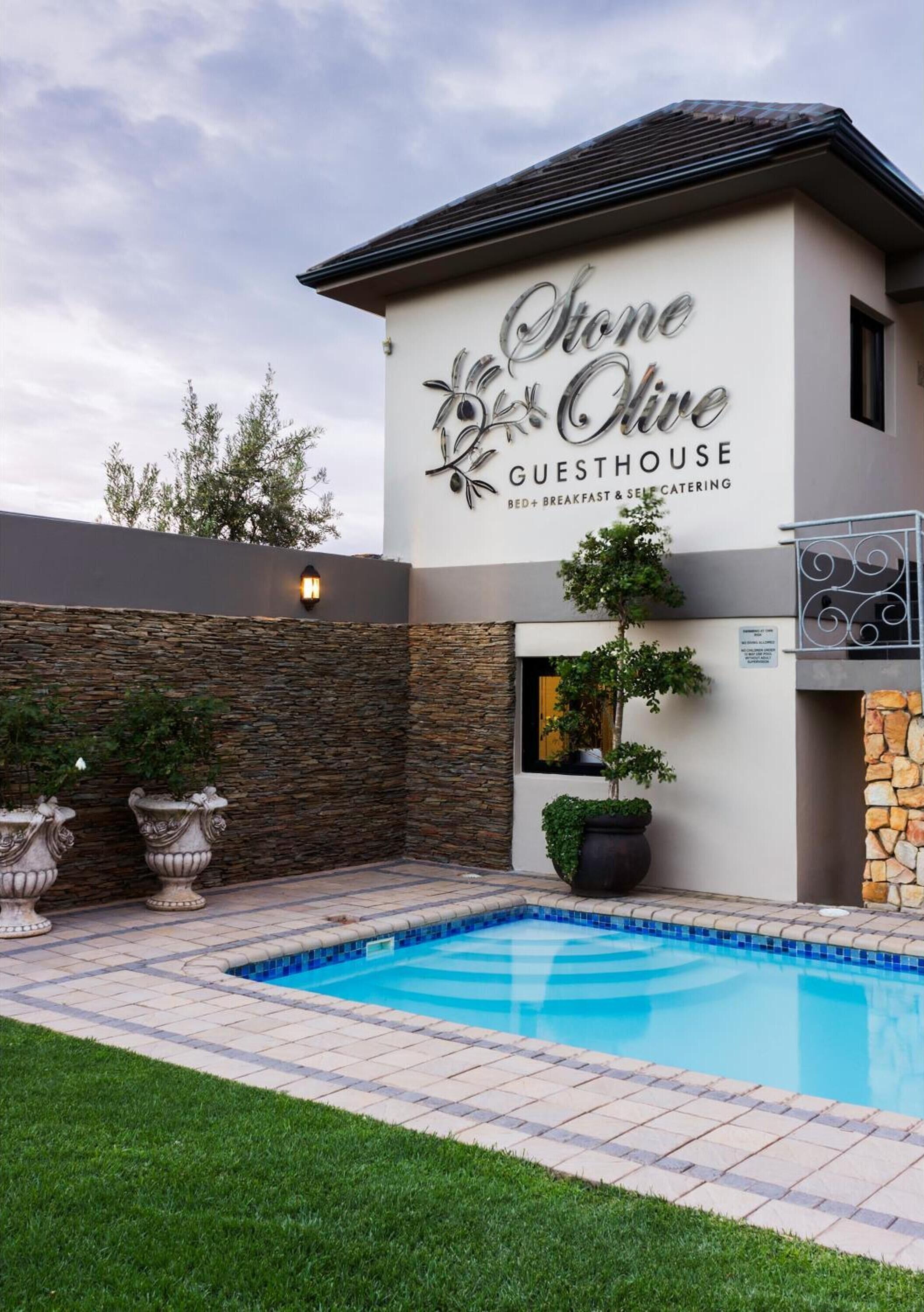 Uma casa de hóspedes moderna com piscina, muro de pedra e plantas em vasos.
