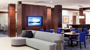Um hall de hotel moderno com um amplo sofá modular, mesas redondas e cadeiras azuis.