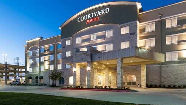 Um hotel Courtyard Marriott com fachada de pedra, várias varandas e uma entrada bem iluminada.