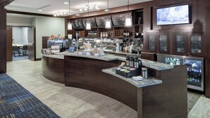 Um lobby de hotel moderno com um balcão de recepção curvo, um café e uma televisão na parede.