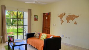 Quarto com uma grande janela, porta de madeira, mapa mundi na parede e sofá com manta.