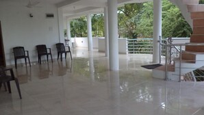 Um espaço interno amplo com piso ladrilhado, várias cadeiras, uma escada e um corrimão.