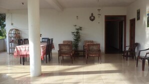 Um espaço interno amplo, com piso ladrilhado, uma mesa de jantar com cadeiras e algumas plantas em vasos.