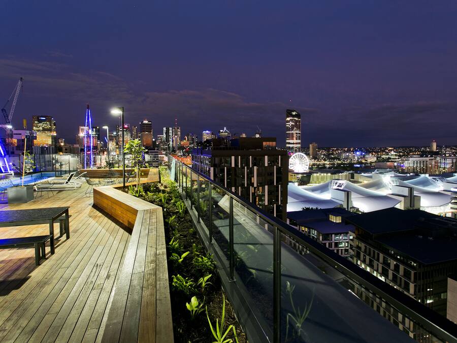Terraço no telhado com vista para o horizonte urbano à noite, destacando edifícios modernos e uma roda gigante.