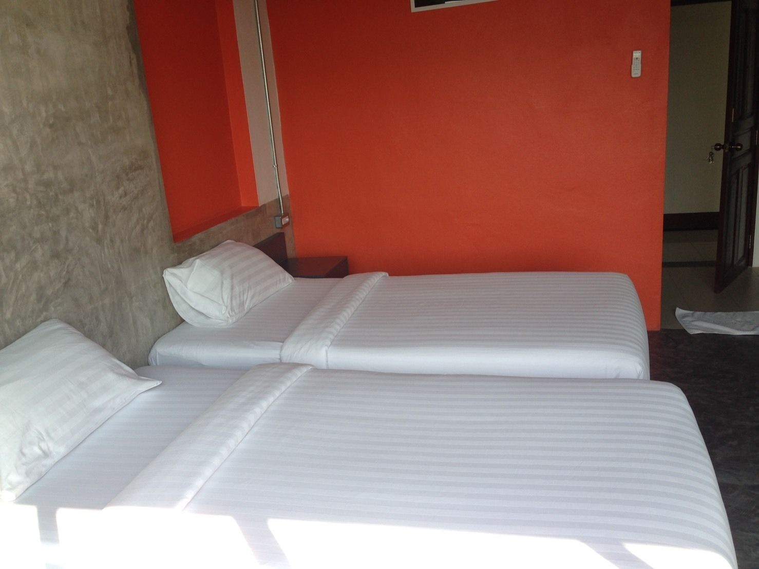 Duas camas de solteiro com roupa de cama branca num quarto com paredes vermelhas e um pilar de concreto.