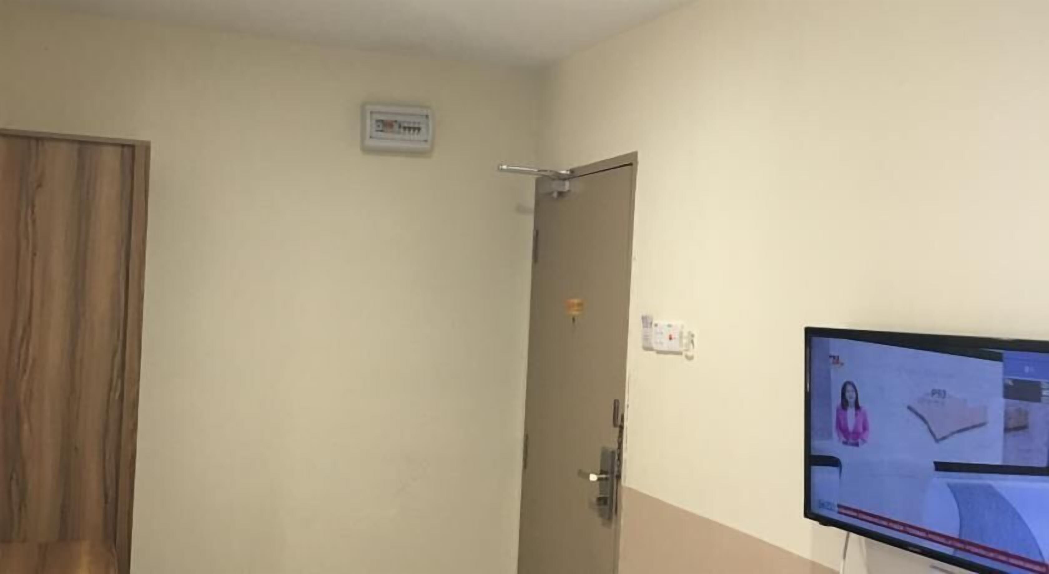Um corredor com uma porta de madeira, um puxador, um interruptor de luz fixado na parede e uma tela de televisão exibindo um objeto rosa.
