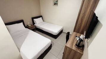 Quarto de hotel com duas camas, uma escrivaninha de madeira, uma cadeira, uma mesinha, telefone e televisão.