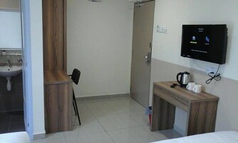Quarto de hotel com escrivaninha de madeira, televisão fixada na parede, pia e porta que dá para outro aposento.