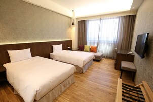 Quarto de hotel com duas camas, um sofá, uma TV e piso de madeira.