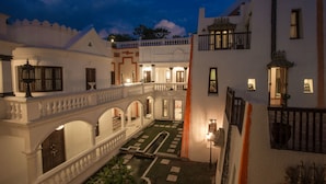 Um pátio central com um espelho de água, rodeado por edifícios brancos com varandas e arcos.
