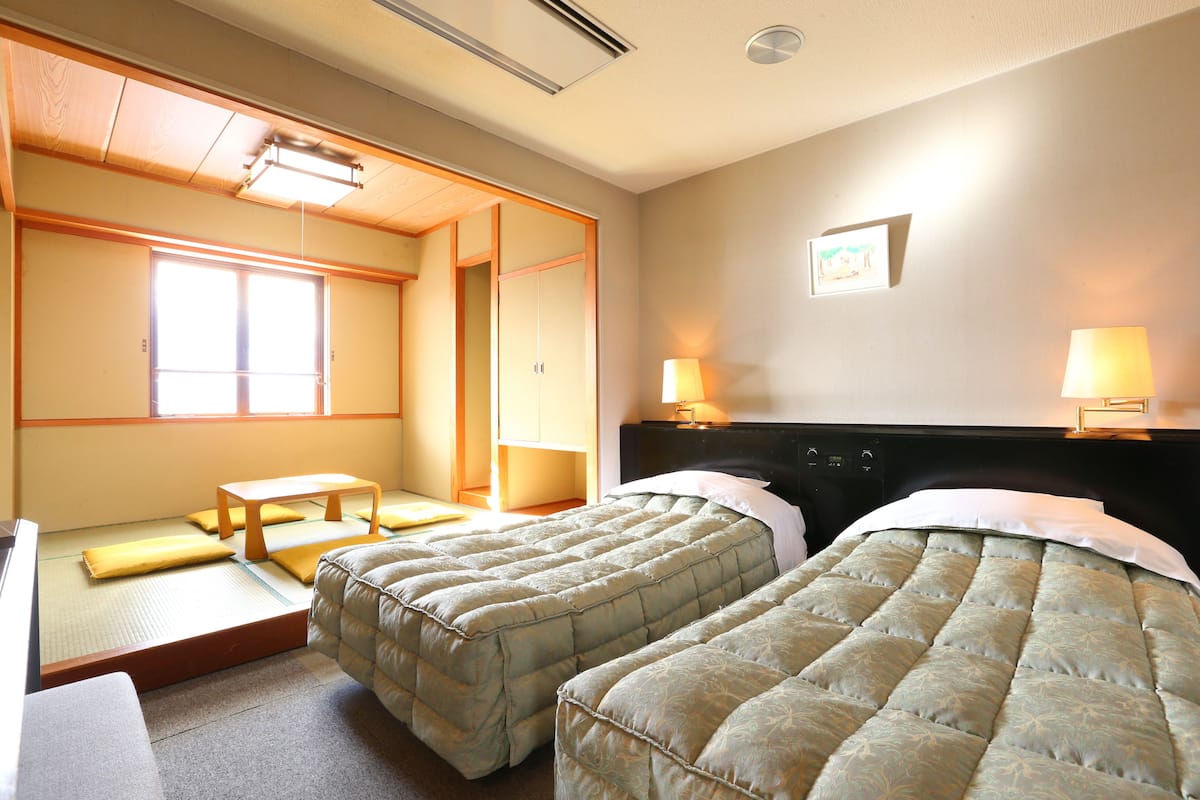 Quarto de hotel com duas camas, uma mesinha e um futon.