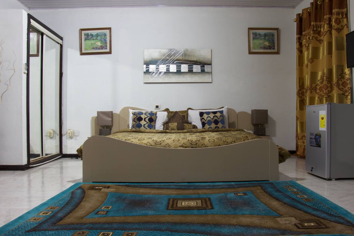 Quarto com cama, tapete, frigorífico e duas pinturas na parede.