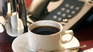 Uma chávena de café sobre um pires, com uma colher, um telefone, um teclado e uma caneta numa mesa de madeira.