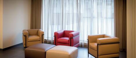 Quarto de hotel moderno com sofá modular, duas poltronas e uma poltrona vermelha de destaque.