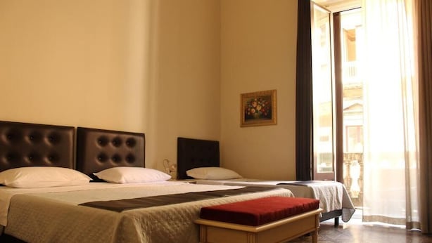 Quarto de hotel com duas camas, um banco, um quadro e vista para o exterior.