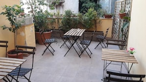 Um pátio com mesa e cadeiras de madeira, plantas em vasos e uma cerca de metal.
