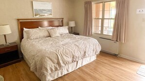 Quarto com cama de madeira, mesa de cabeceira, luminária, janela com cortinas e um quadro na parede.