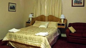 Quarto de hotel com uma cama de solteiro, duas mesas de cabeceira com luminárias, uma poltrona vermelha e um quadro na parede.