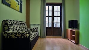 Sala de estar com sofá estampado, televisão em móvel de madeira e uma grande janela com cortinas.