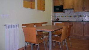 Uma sala de jantar com mesa e cadeiras, uma cozinha com armários de madeira e painel de azulejos.