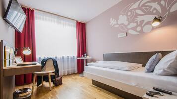 Quarto de hotel moderno com cama, escrivaninha, cadeira e televisão fixada na parede.
