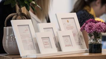 Exposição de certificados ou prémios emoldurados sobre uma mesa de madeira, acompanhada por uma planta em vaso e um vaso com flores.