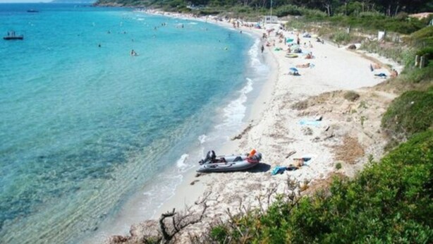 Uma praia com águas turquesa cristalinas, um areal e um relevo montanhoso ao fundo.