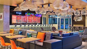 Uma área de bar moderna com balcão, assentos e uma tela de televisão exibindo conteúdo colorido.