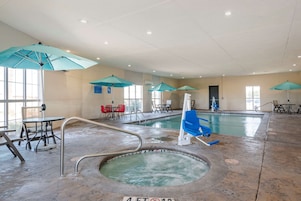 Uma área de piscina interna com várias pistas de natação, uma banheira de hidromassagem e áreas de estar com guarda-sóis.