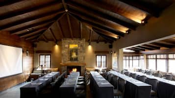 Uma sala de conferências com mesas longas, cadeiras, uma lareira de pedra e vigas de madeira.