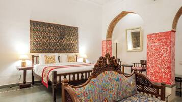 Quarto com cama grande, cabeceira de madeira, sofá estampado e cortina vermelha.