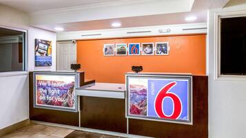 Bancada de recepção de hotel com uma placa de número 6, um visor digital e uma série de fotografias emolduradas na parede.