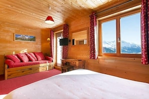 Quarto de cabana de madeira com uma cama, um sofá vermelho, uma escrivaninha e uma televisão.