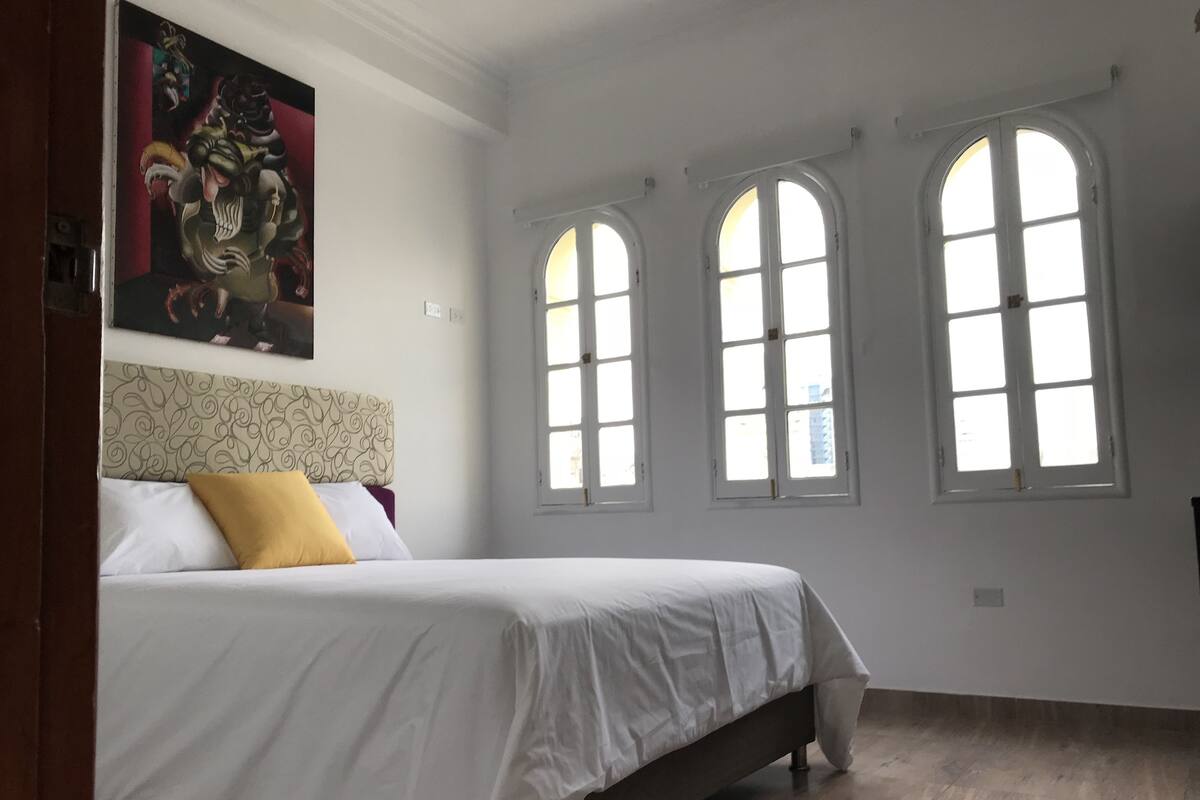 Quarto com uma cama, uma janela grande e um quadro na parede.