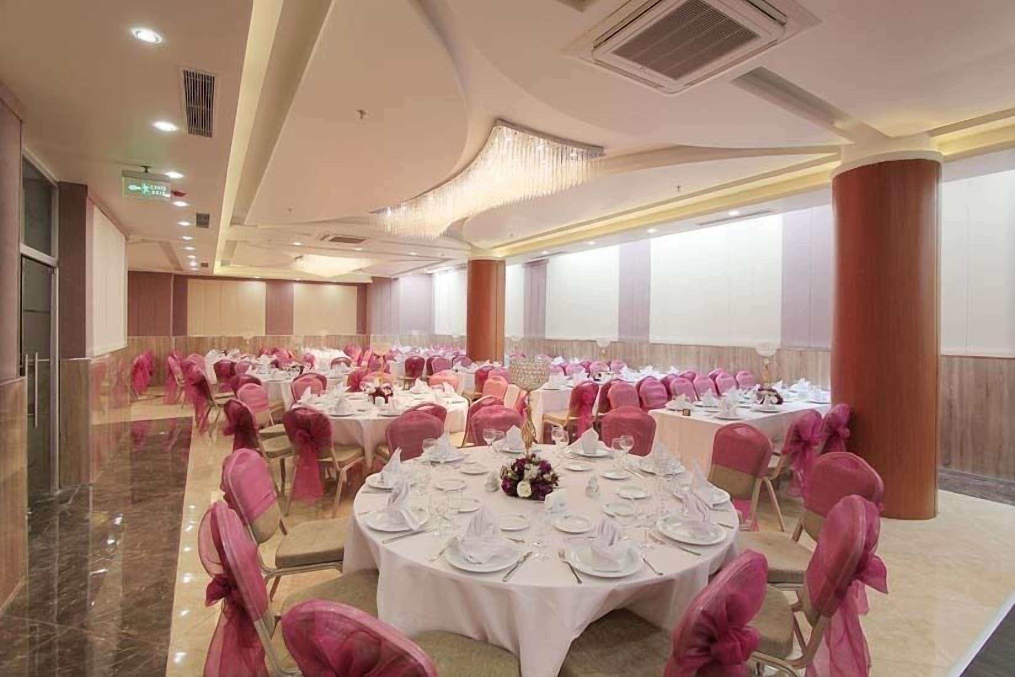 Uma sala de banquetes com mesas redondas dispostas para refeições, capas rosa para as cadeiras e um piso de mármore polido.