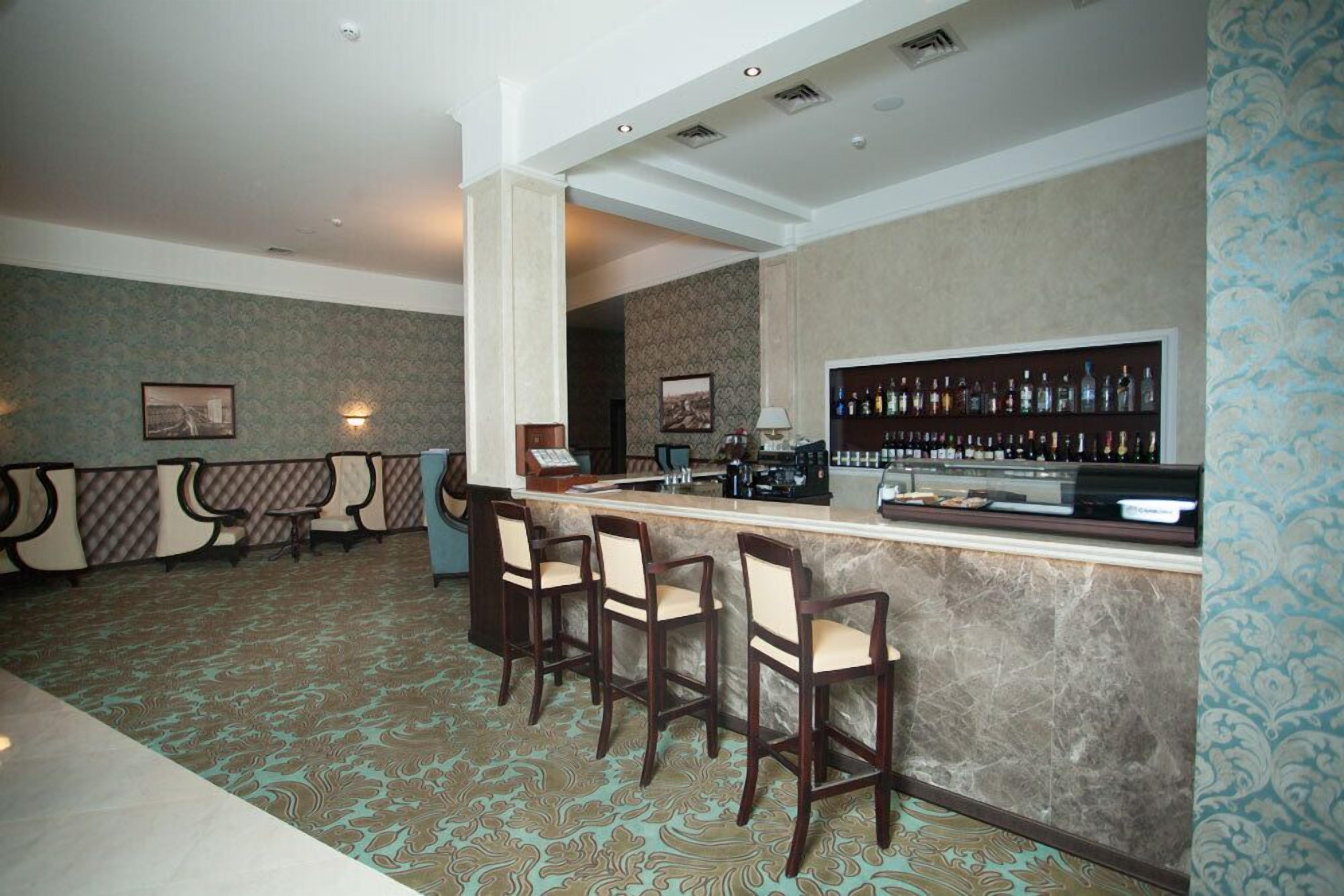 Uma área de bar com balcão de mármore, banquetas e uma parede de garrafas de bebidas.