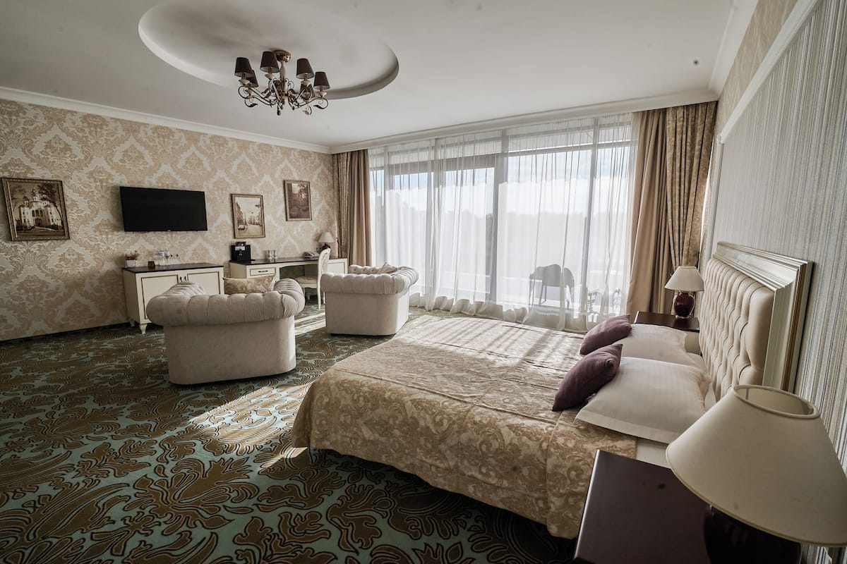 Quarto de hotel com uma cama grande, duas poltronas, uma escrivaninha e uma televisão.